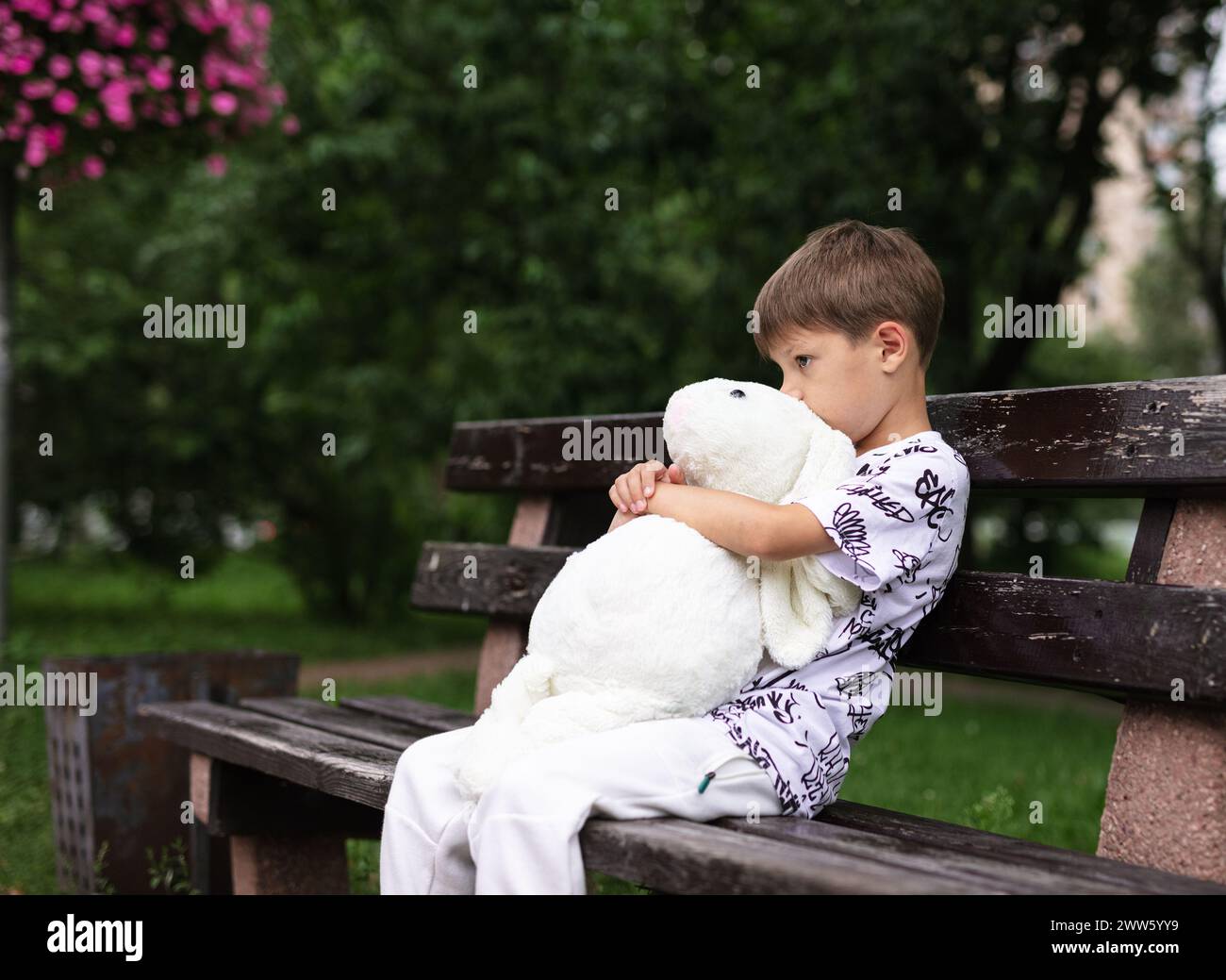Young boy hugging his toy bunny and sitting on bench in park Stock ...