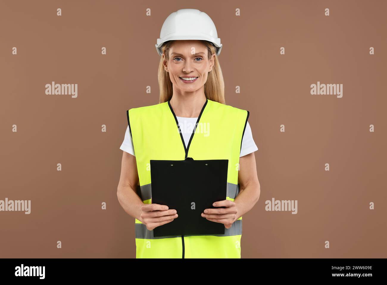Engineer in hard hat holding clipboard on brown background Stock Photo ...