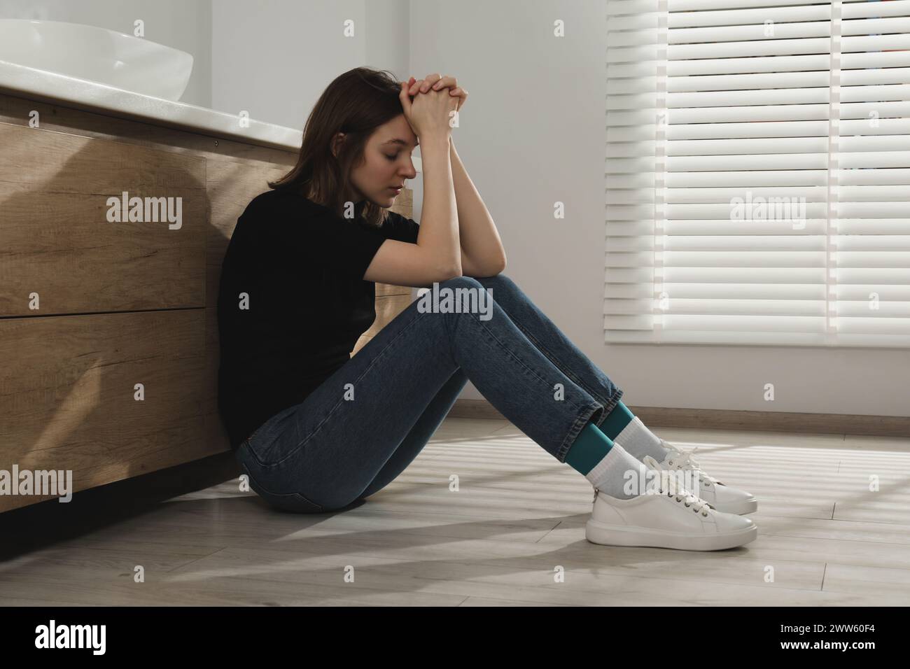Sad young woman sitting on floor indoors Stock Photo - Alamy