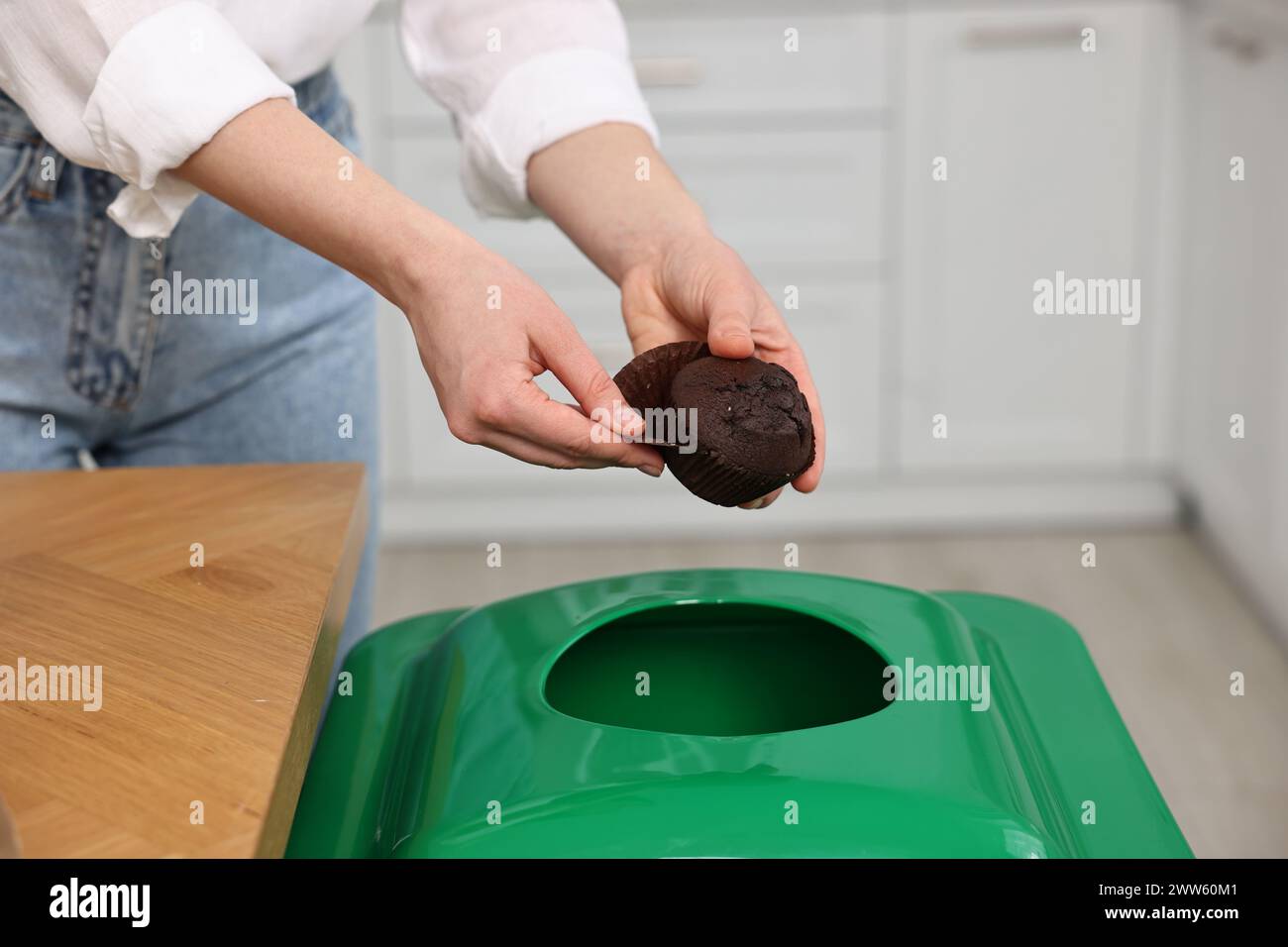 Garbage sorting. Woman throwing muffin liner into trash bin indoors ...