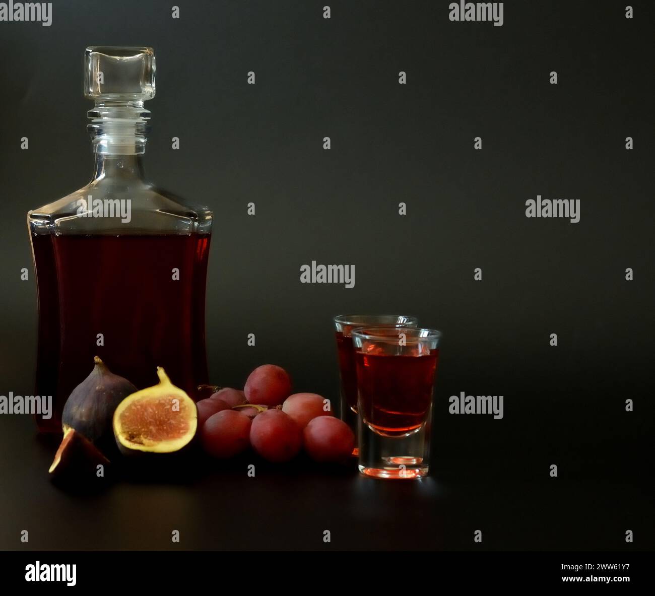 Fig-grape liqueur in a bottle and two glasses on a black background ...
