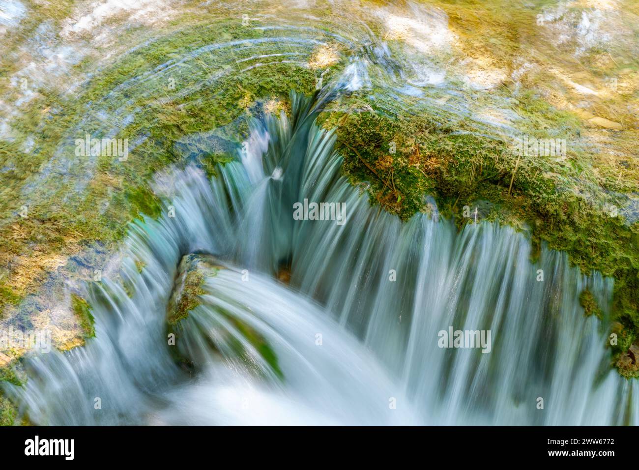 Converging edge of landform with water streaming over edge into pond ...