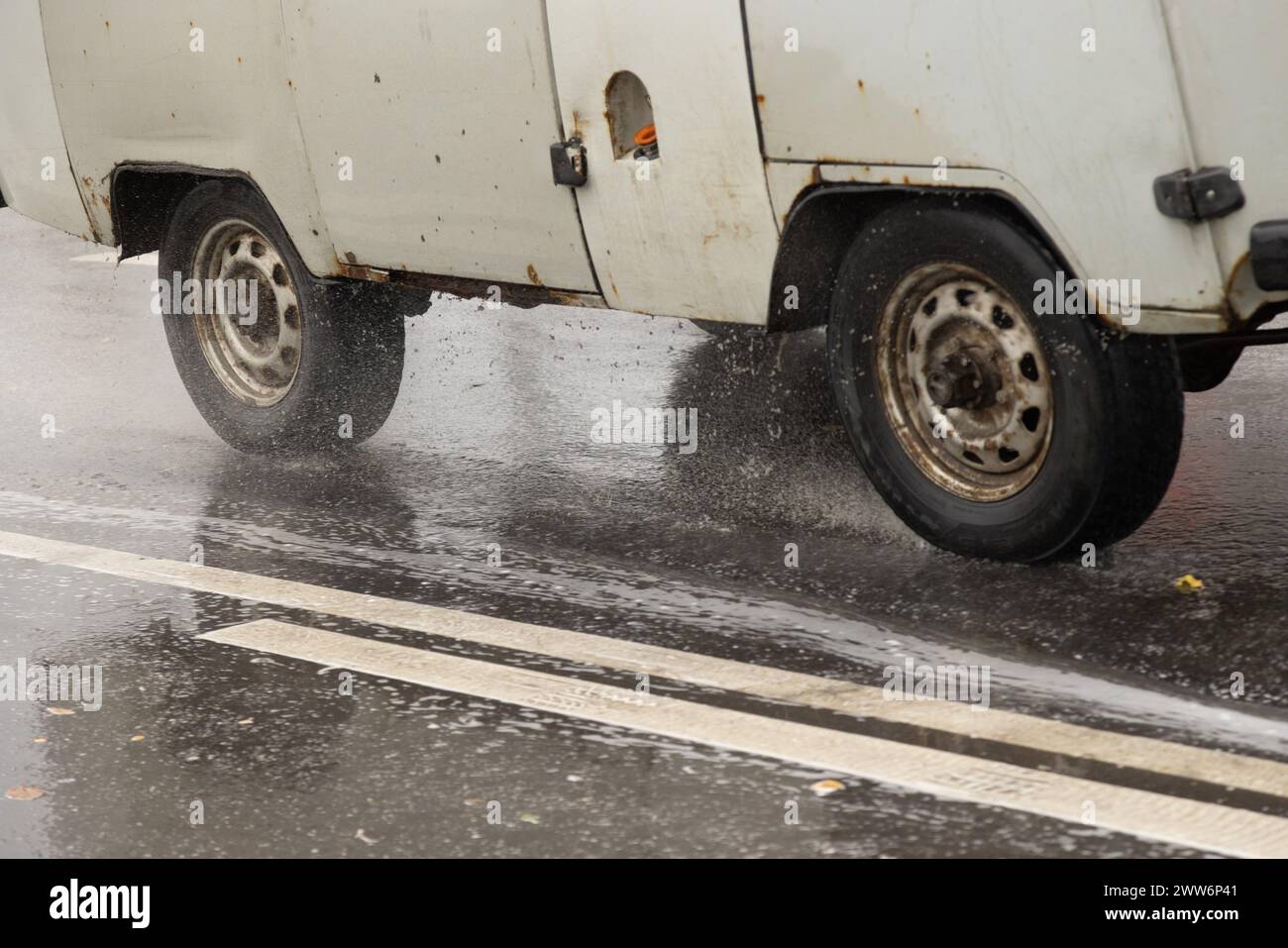 old rusty soviet minivan driving on the wet asphalt road during heavy ...