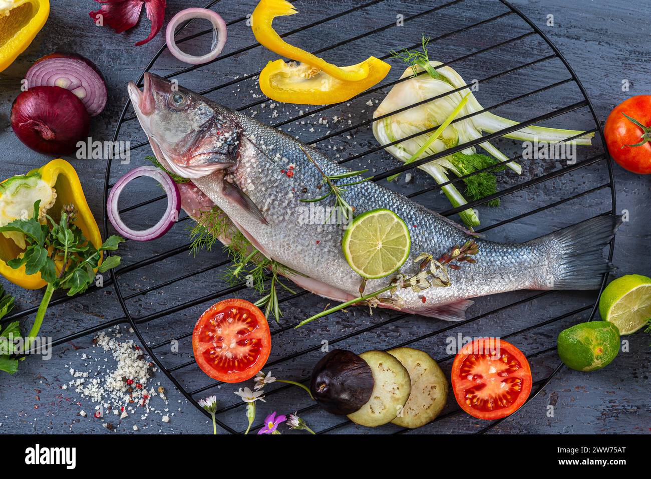 Sea bass placed on a barbecue grill surrounded by vegetables, before ...
