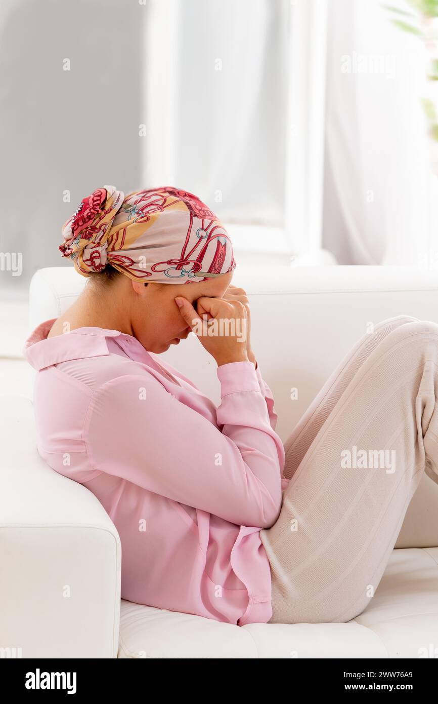 Woman wearing a headscarf, in profile, curled up on the sofa, her fists ...