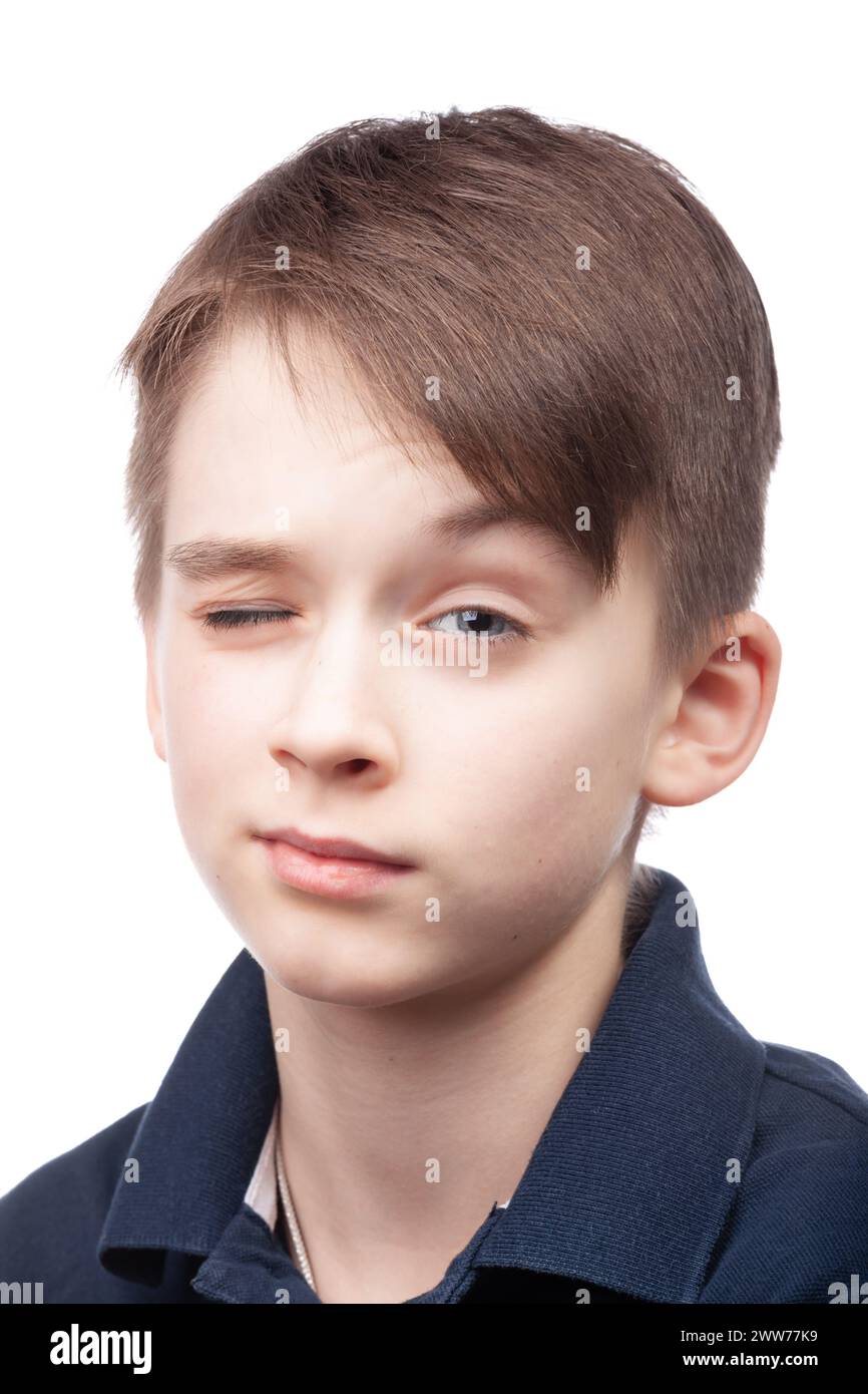 A young boy wearing blue polo shirt playfully winks with one eye closed ...