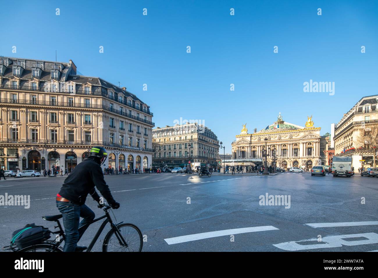 A cyclist crosses an intersection at Pariss Opera Square under a clear ...