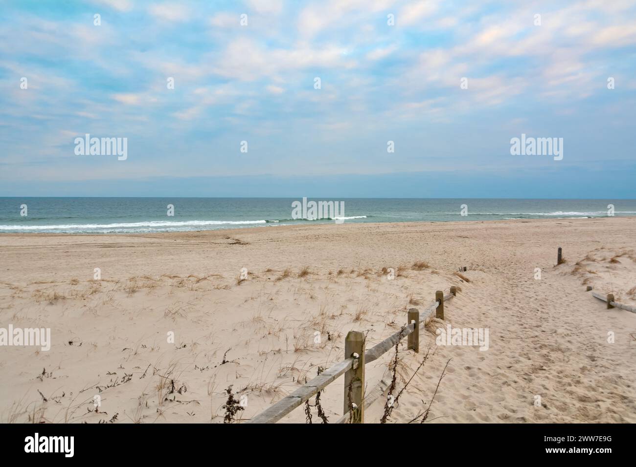 The image captures a sandy trail leading to a serene beach, with a ...
