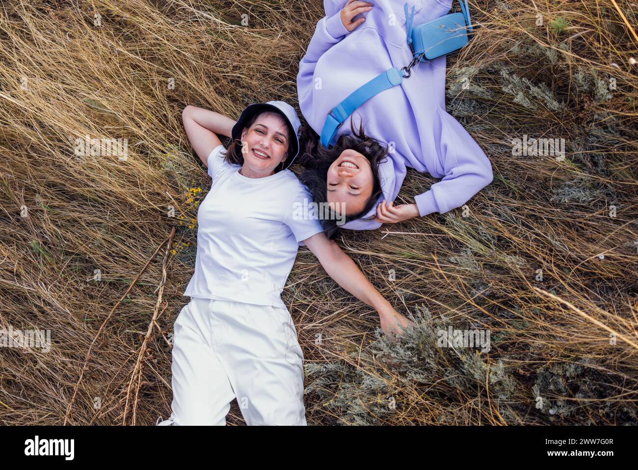 Two multiethnic friends are lying on the dry grass and laughing. Young ...