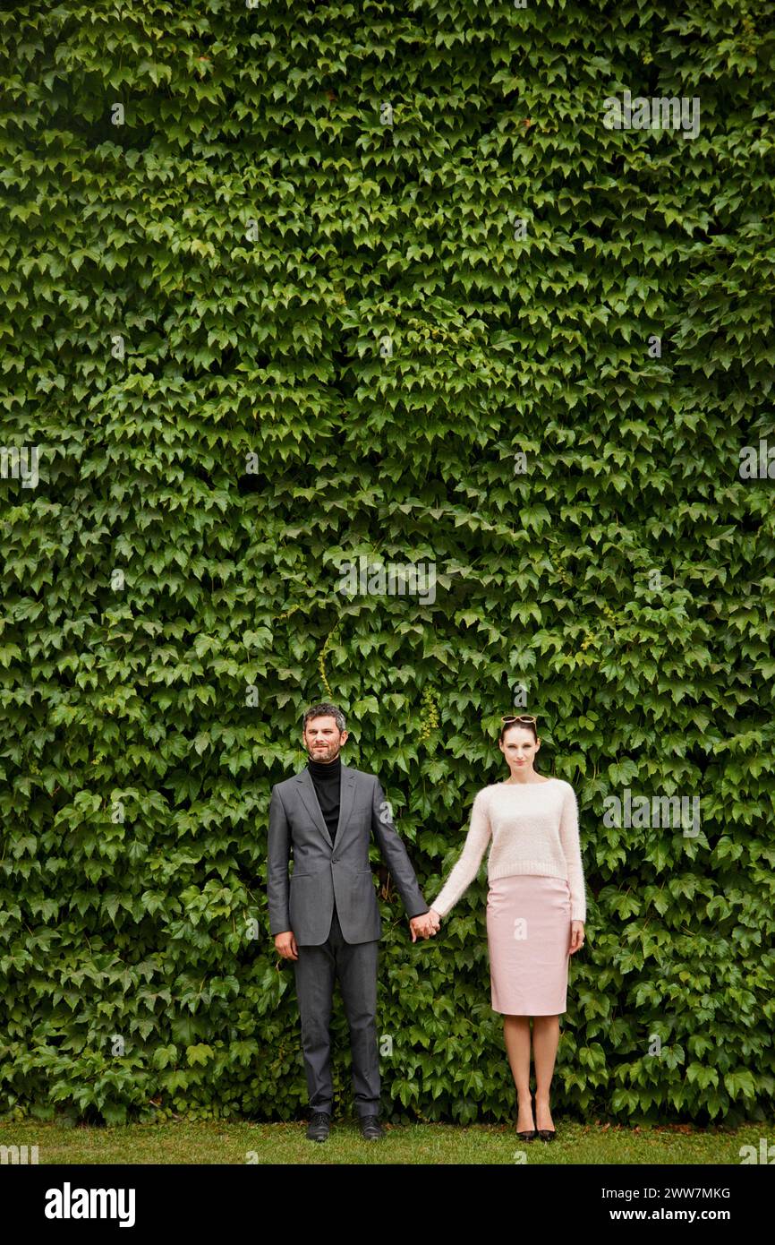 Couple Holding Hands Standing in front of Green Leafy Hedge Stock Photo ...
