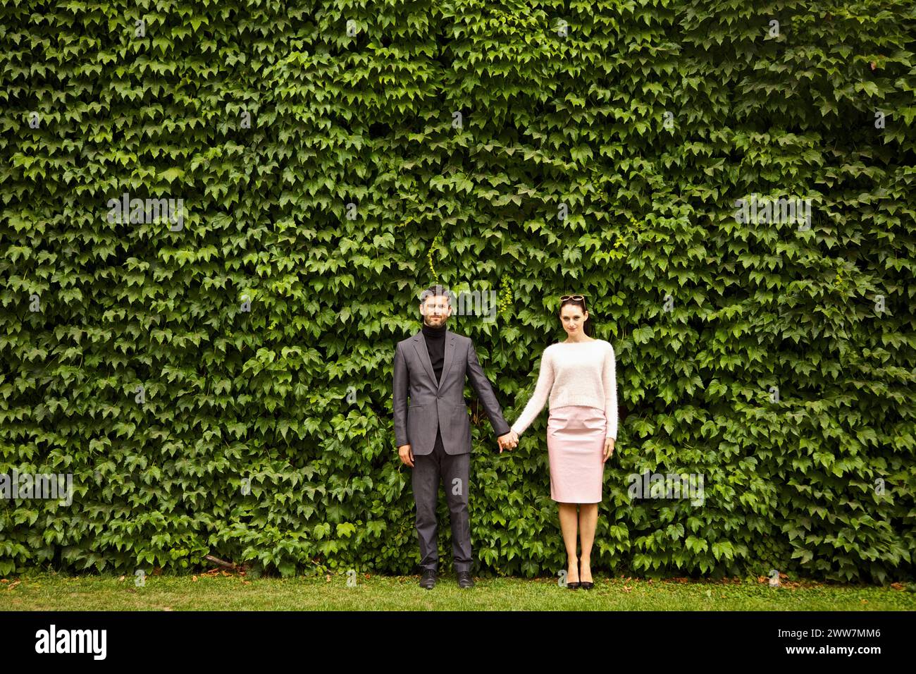 Couple Holding Hands Standing in front of Green Leafy Hedge Stock Photo ...