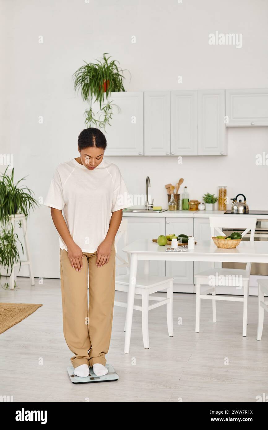 african american woman in casual attire standing on scale in kitchen ...