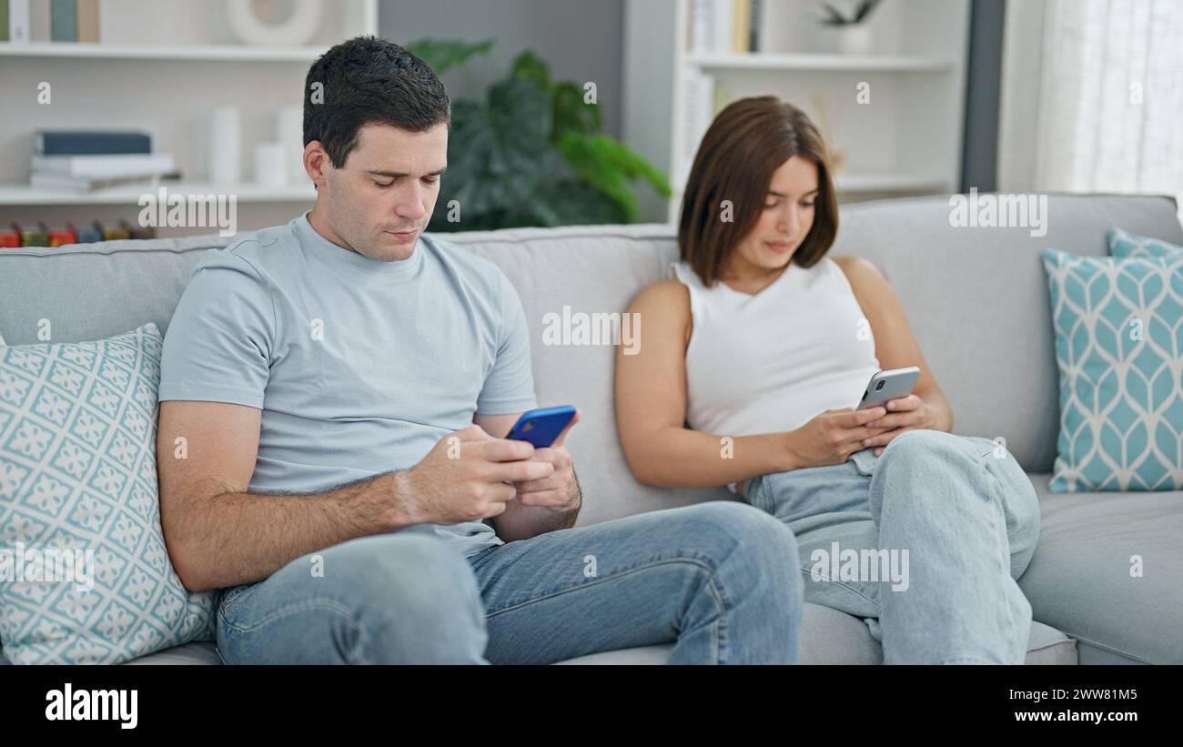 Beautiful couple sitting on sofa together using smartphones at home ...