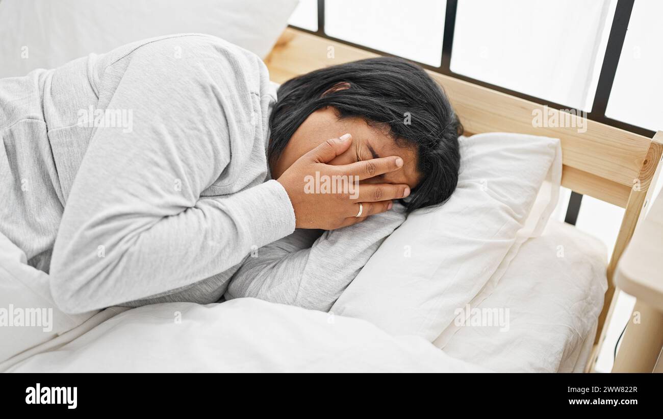 A distressed middle-aged woman lying in bed with her hand on her ...