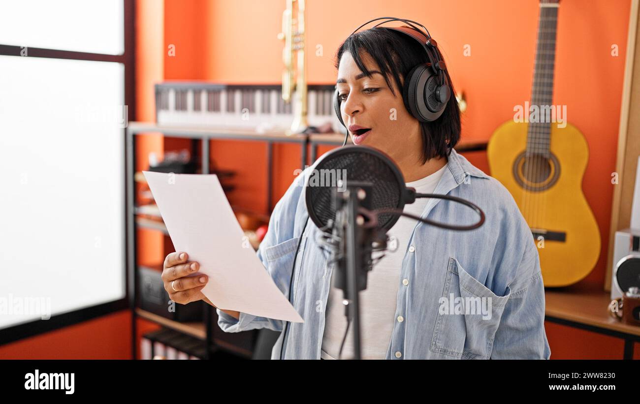 Hispanic woman singing into microphone in music studio with guitar ...