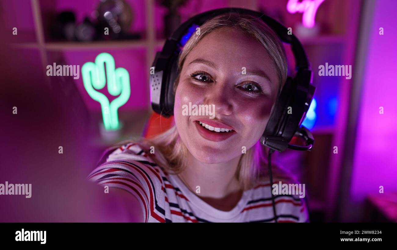 Smiling young woman with headphones enjoying time in a vibrant gaming ...