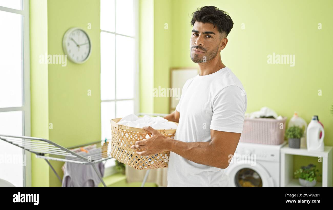 Handsome young hispanic man holding laundry basket in a bright green ...