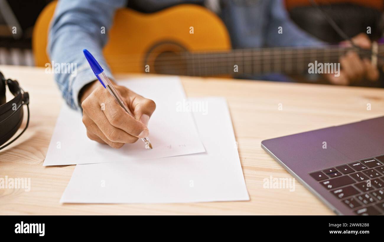 Hispanic man writing music studio notes with guitar and laptop Stock ...