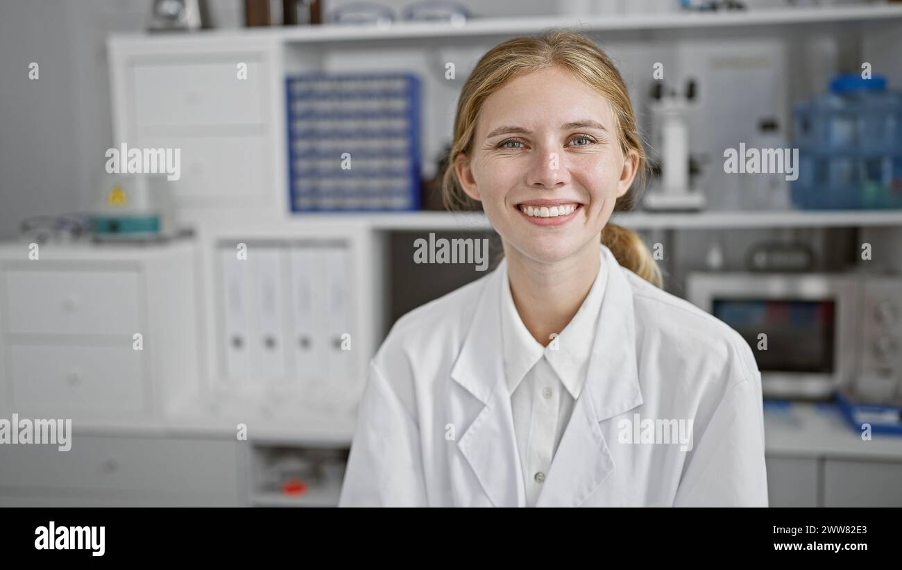 A smiling blonde woman in a white lab coat inside a well-equipped ...