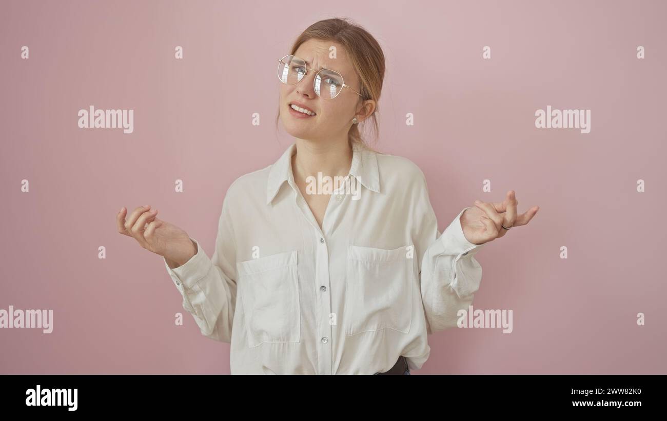 A confused young woman with glasses against a pink background ...