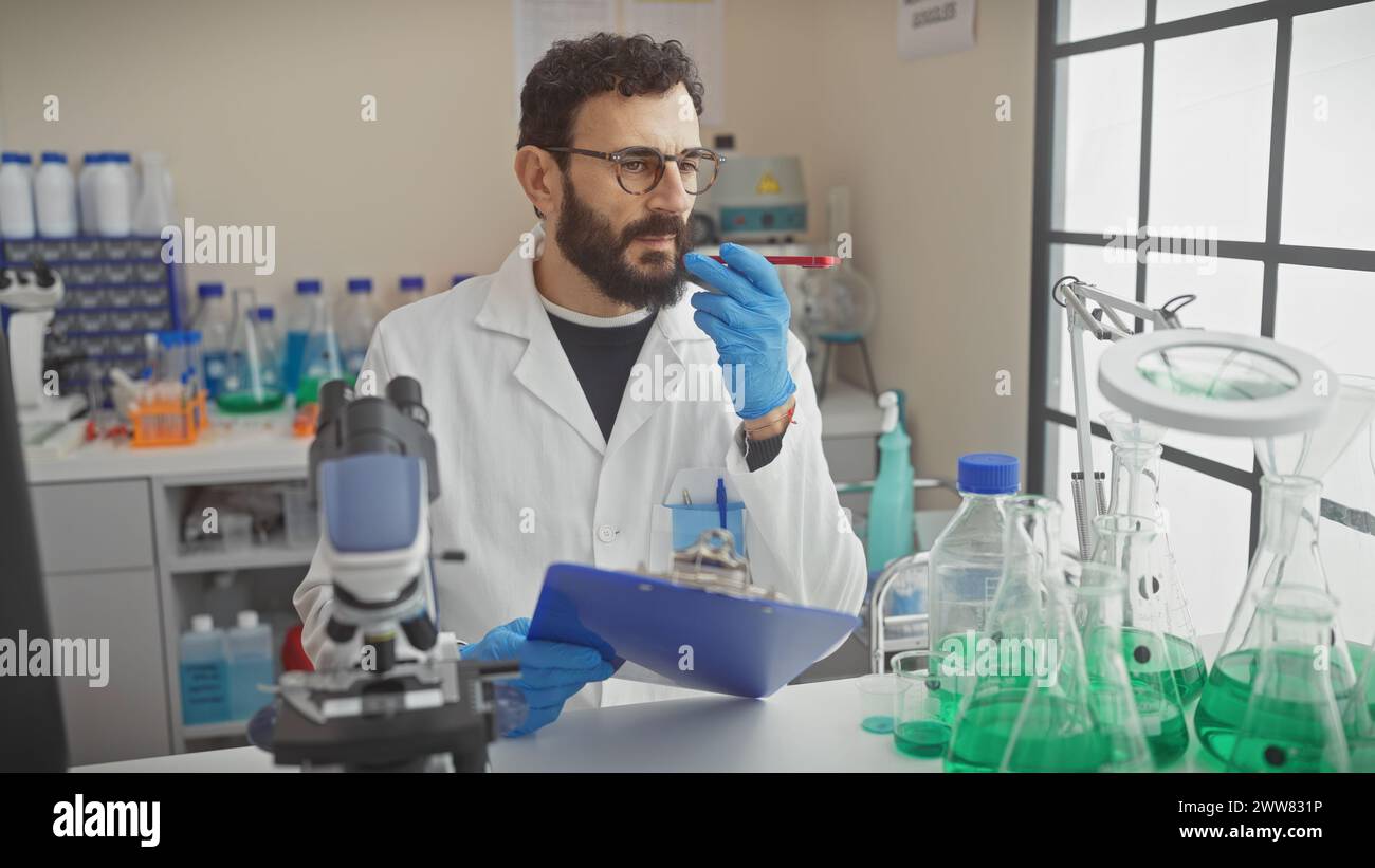 Middle-aged bearded man in lab coat examines a test tube inside a well ...