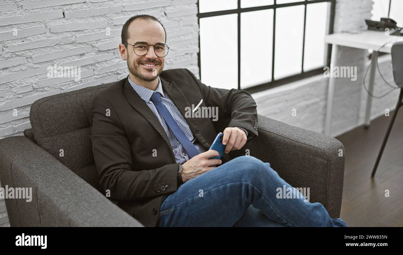 Smiling bald man with beard in suit sitting casually on couch in modern ...