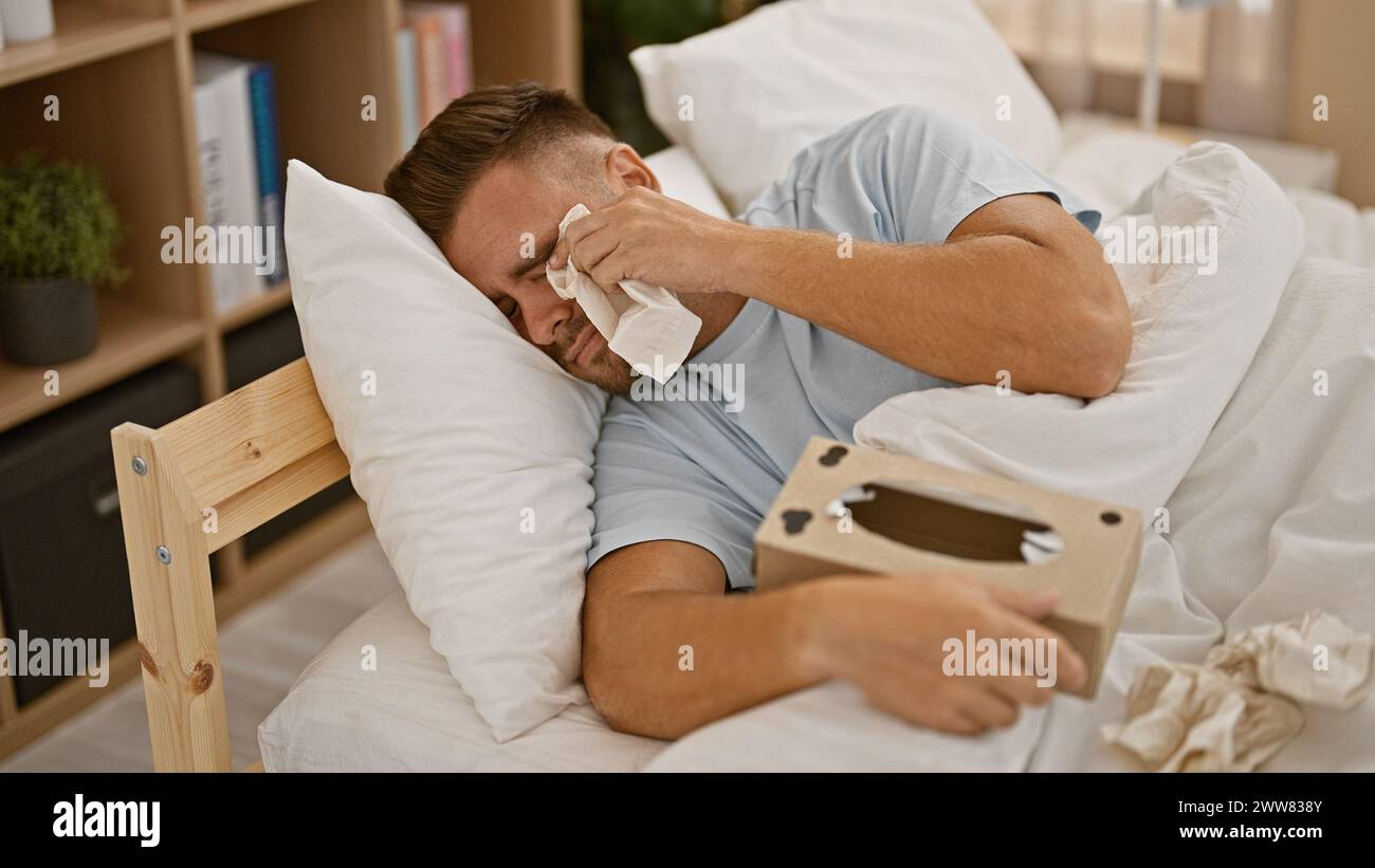 A young hispanic man crying in bed, with tissues at home, portraying ...