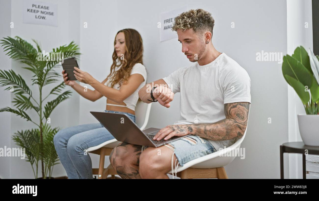 A man checking his watch and a woman reading a tablet sit separately in ...