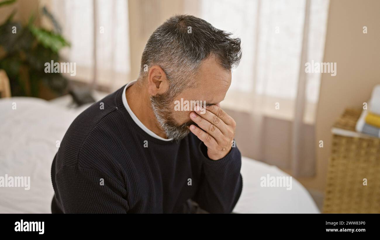 Mature hispanic man rubbing eyes with grey beard in indoor bedroom ...