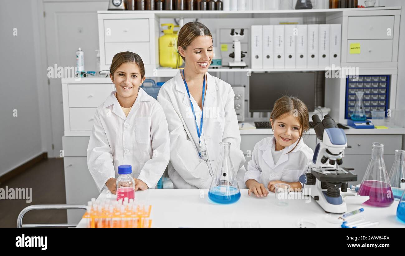 A smiling woman and two girls wearing lab coats sit at a science ...