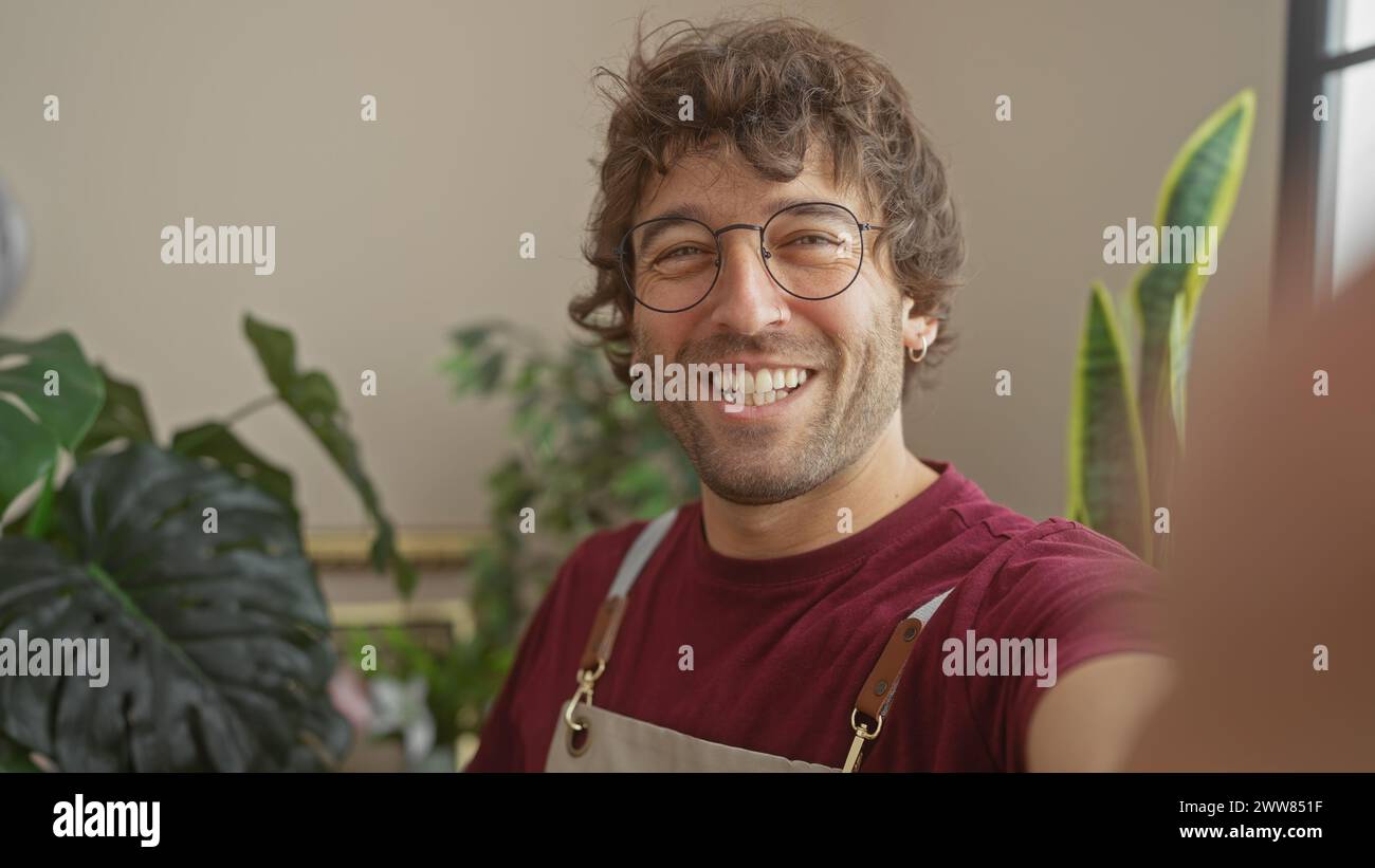 A cheerful man with glasses and a beard takes a selfie in a green plant ...