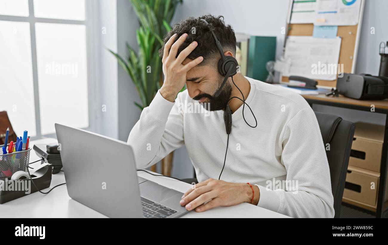 A stressed hispanic man with a beard wearing headphones looks troubled ...