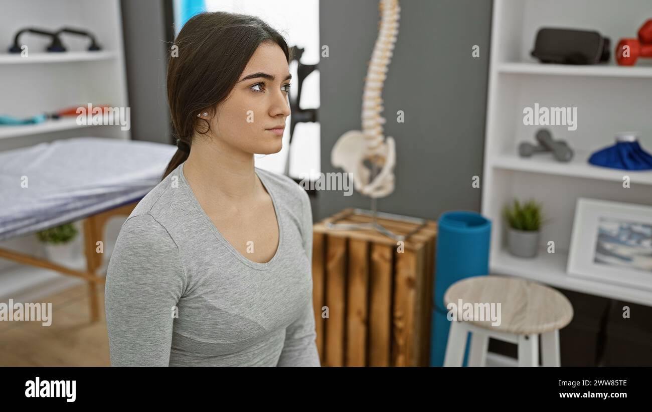 A thoughtful young hispanic woman in a clinic with medical equipment ...