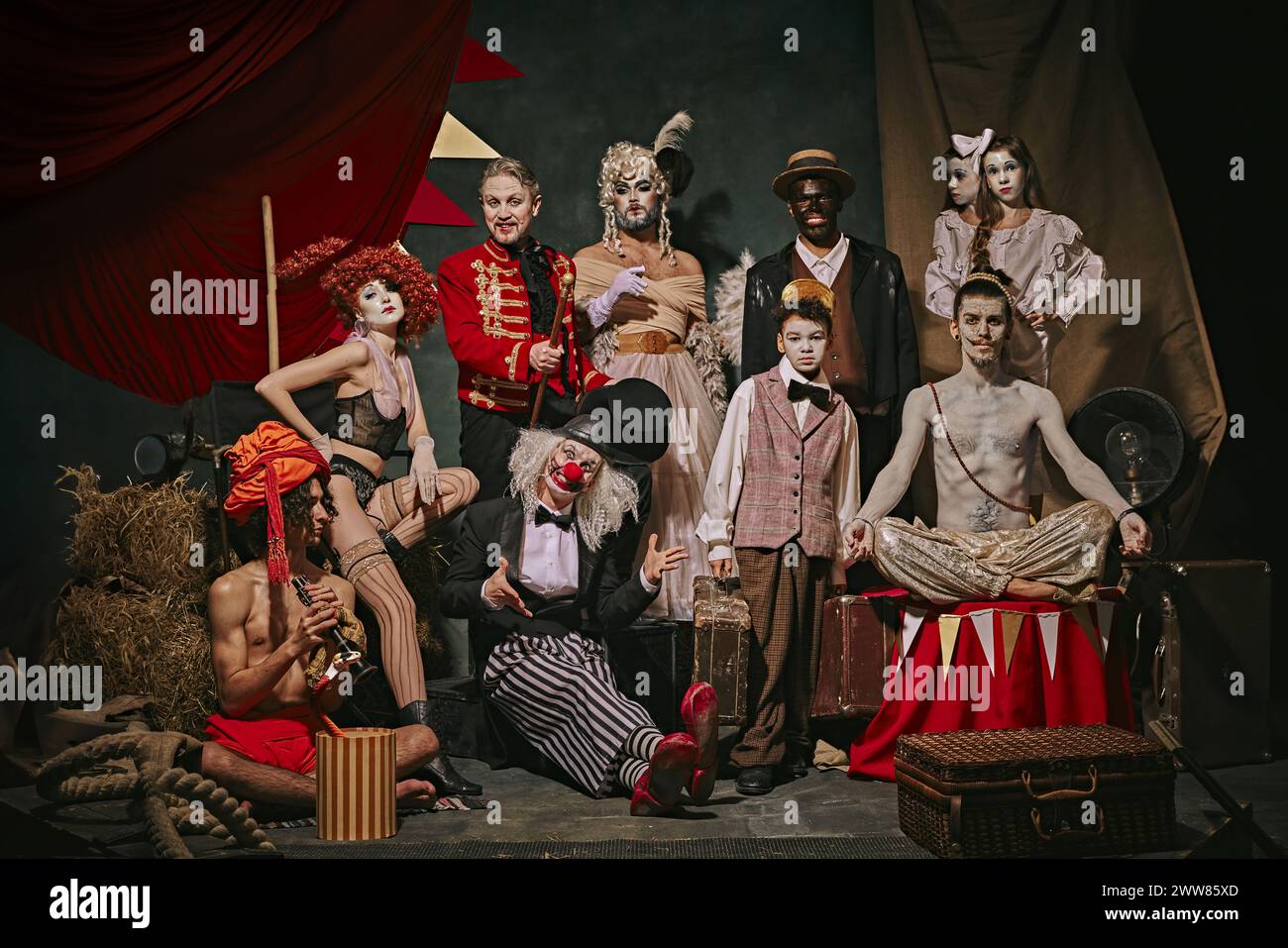 Diverse cast of vintage circus performers poses over dark retro circus backstage background ...