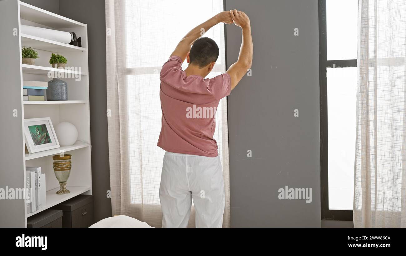 A young man stretching in a well-lit bedroom with a modern decor ...