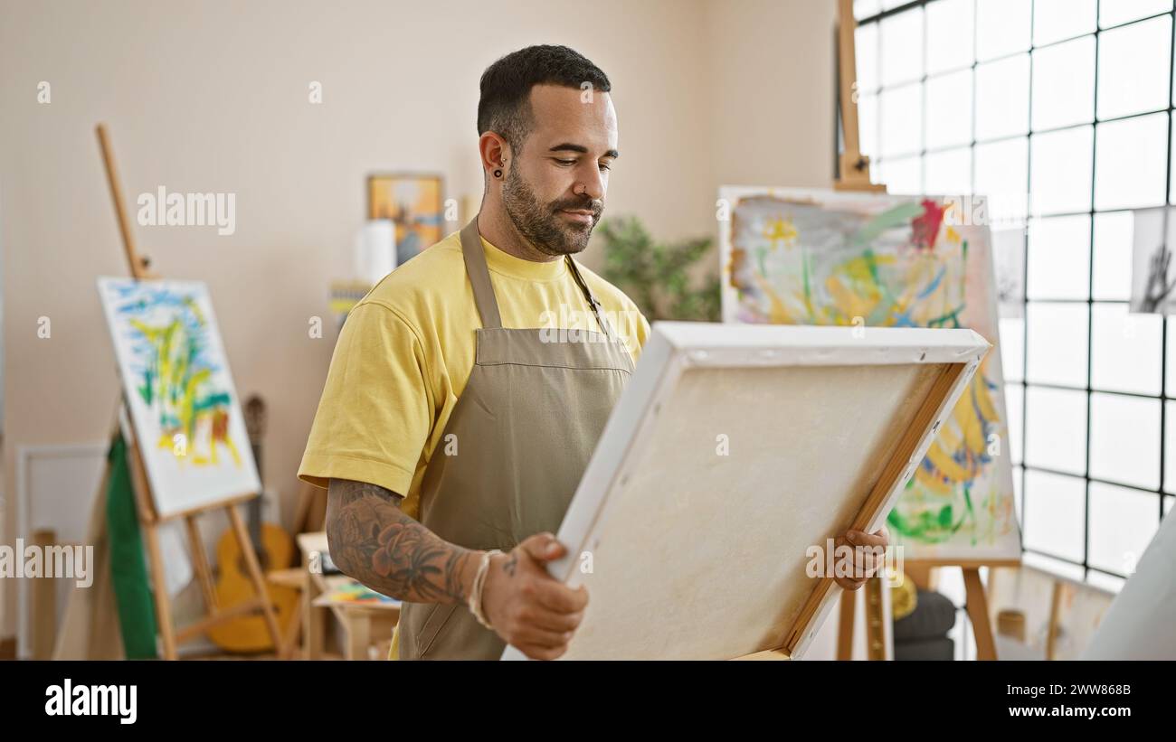 A focused hispanic man examines his painting in a bright art studio ...