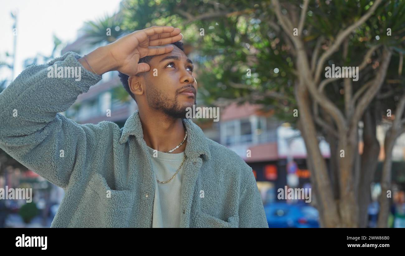 African man shading eyes with hand on a sunlit urban street outdoors ...