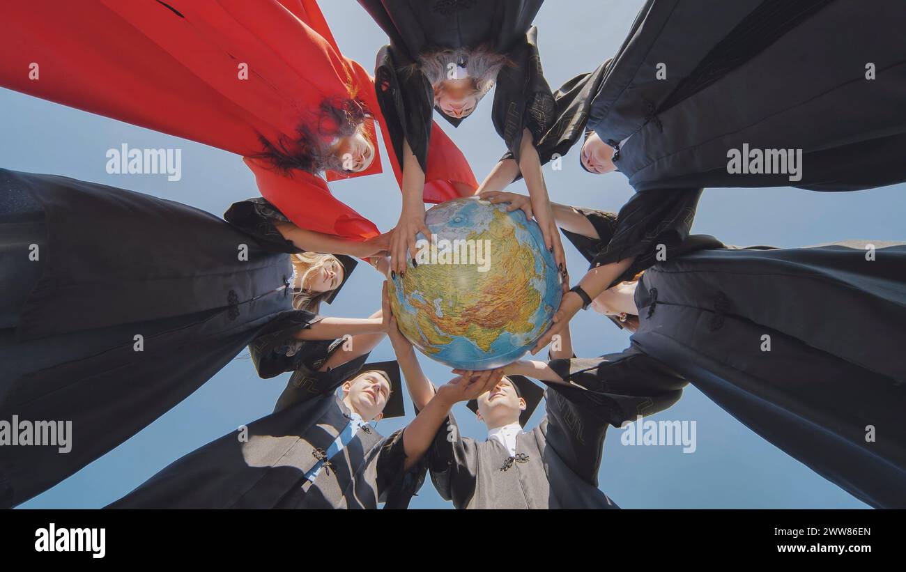 College graduates stand in a circle and hold a geographical globe of ...