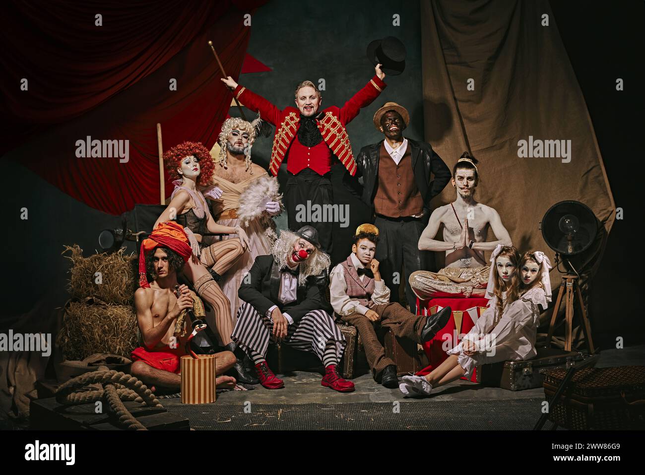 Diverse cast of vintage circus performers poses over dark retro circus backstage background ...