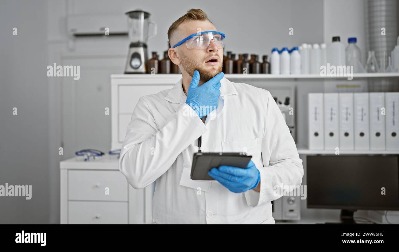 A thoughtful caucasian man in a laboratory wearing gloves, goggles and ...