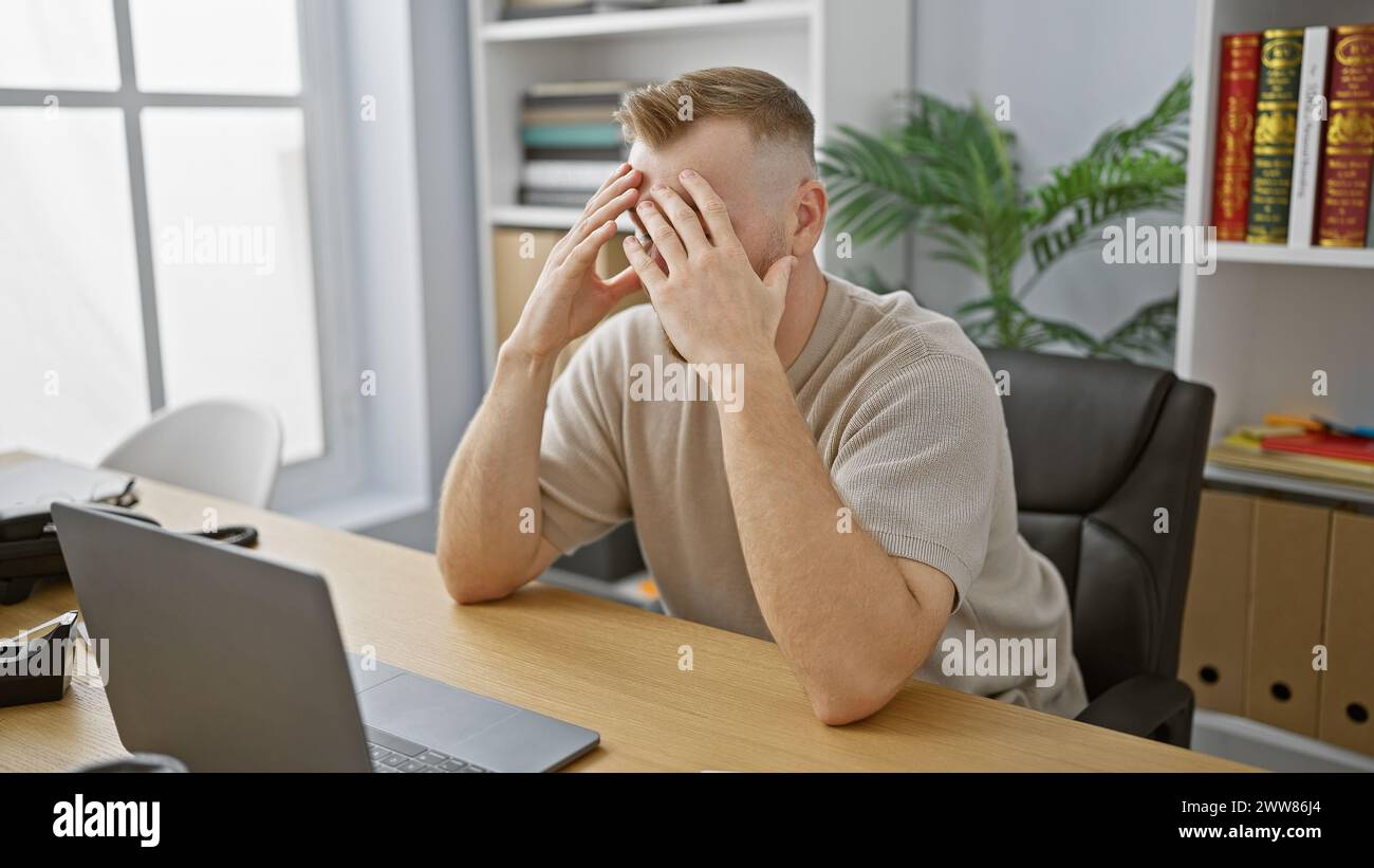 Stressed young man with a beard sitting at an office desk, covering his ...