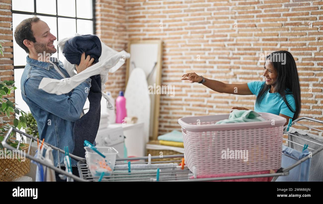 Beautiful couple throwing clothes to each other playing at laundry room ...