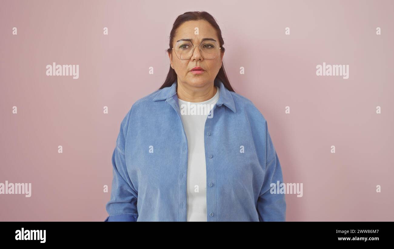 Mature hispanic woman in a denim shirt poses against a solid pink ...