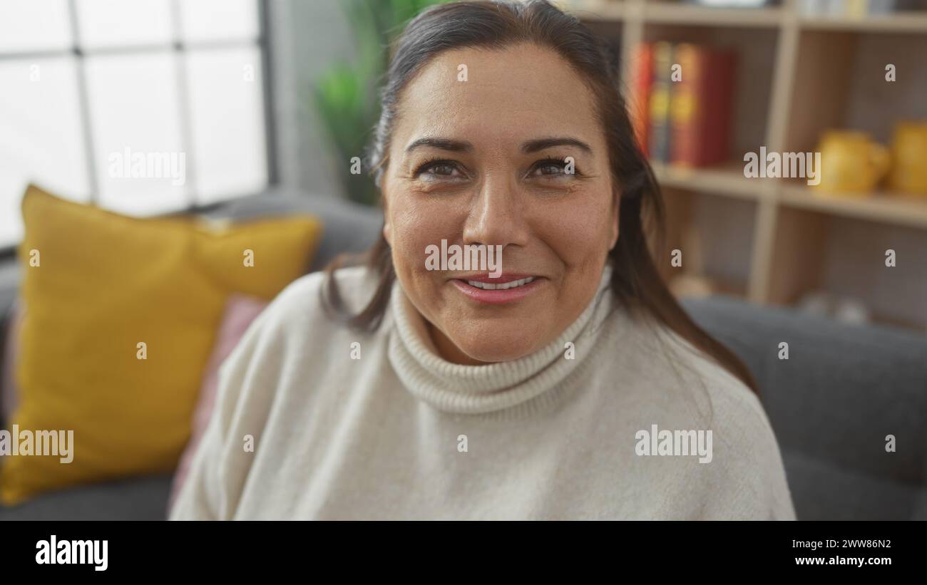 A smiling middle-aged hispanic woman indoors, comfortably sitting in a living room with a cozy ...