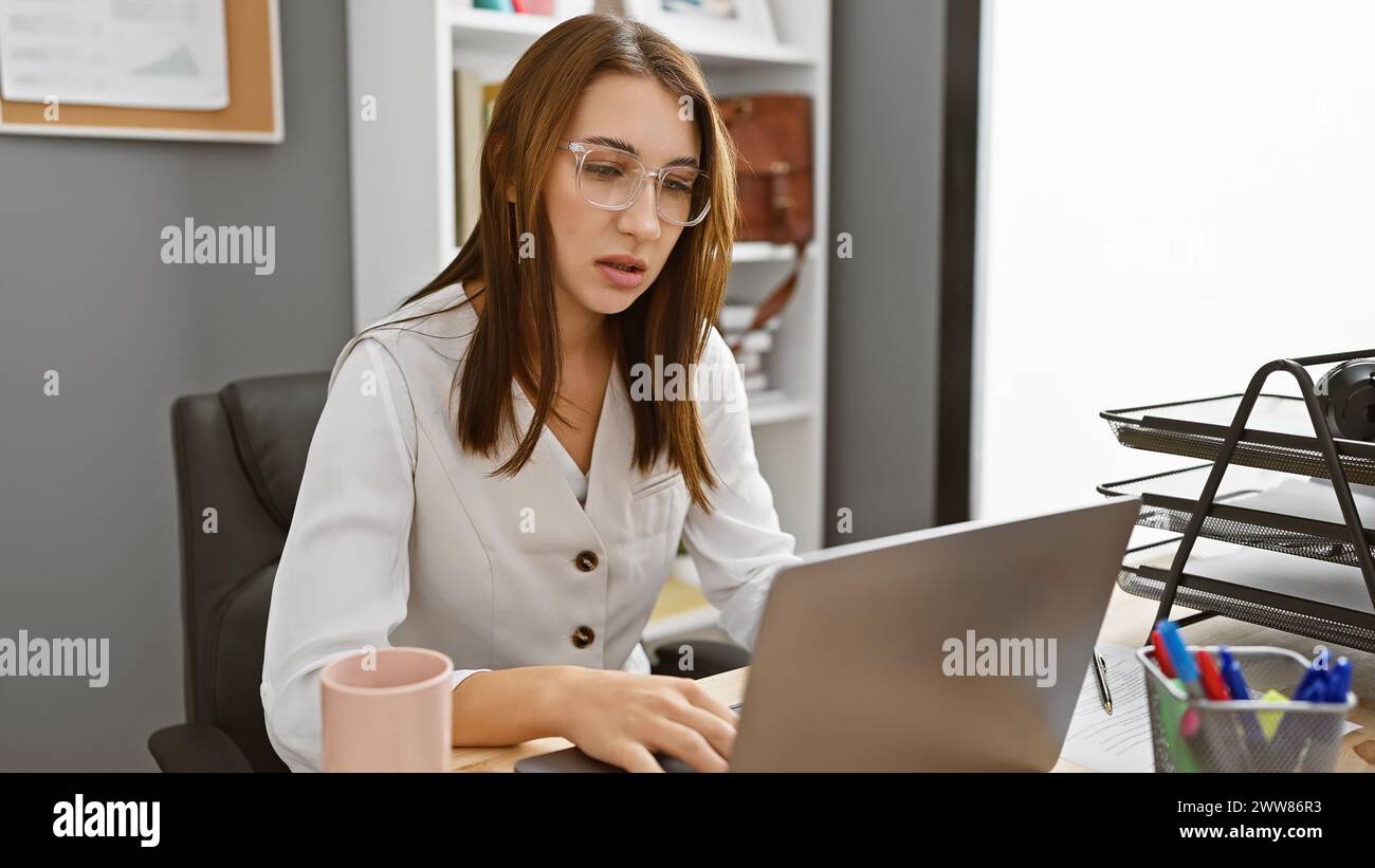 Focused young woman working on laptop in modern office setting ...