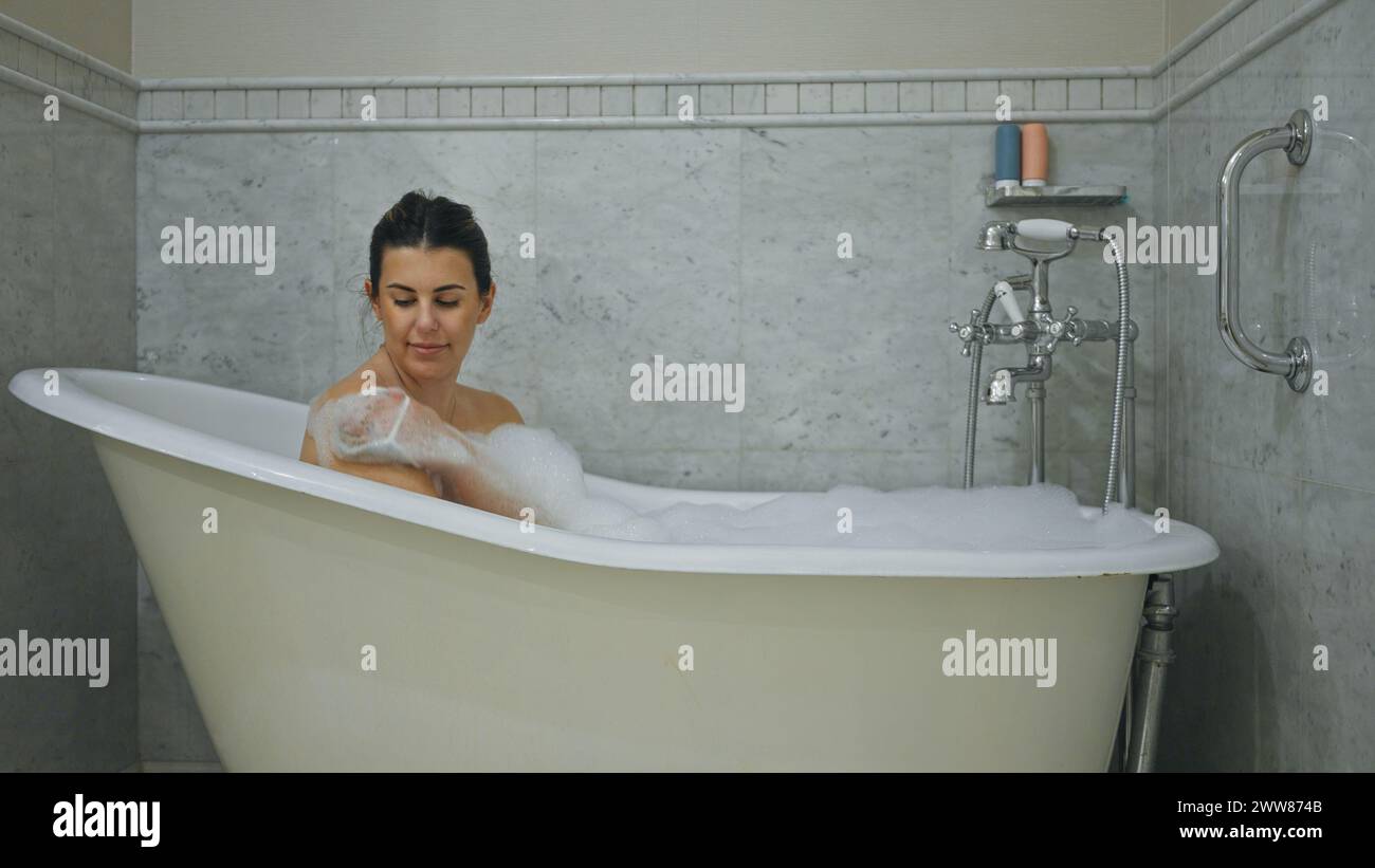 A relaxed young woman enjoying a luxurious bubble bath in a clean, well ...