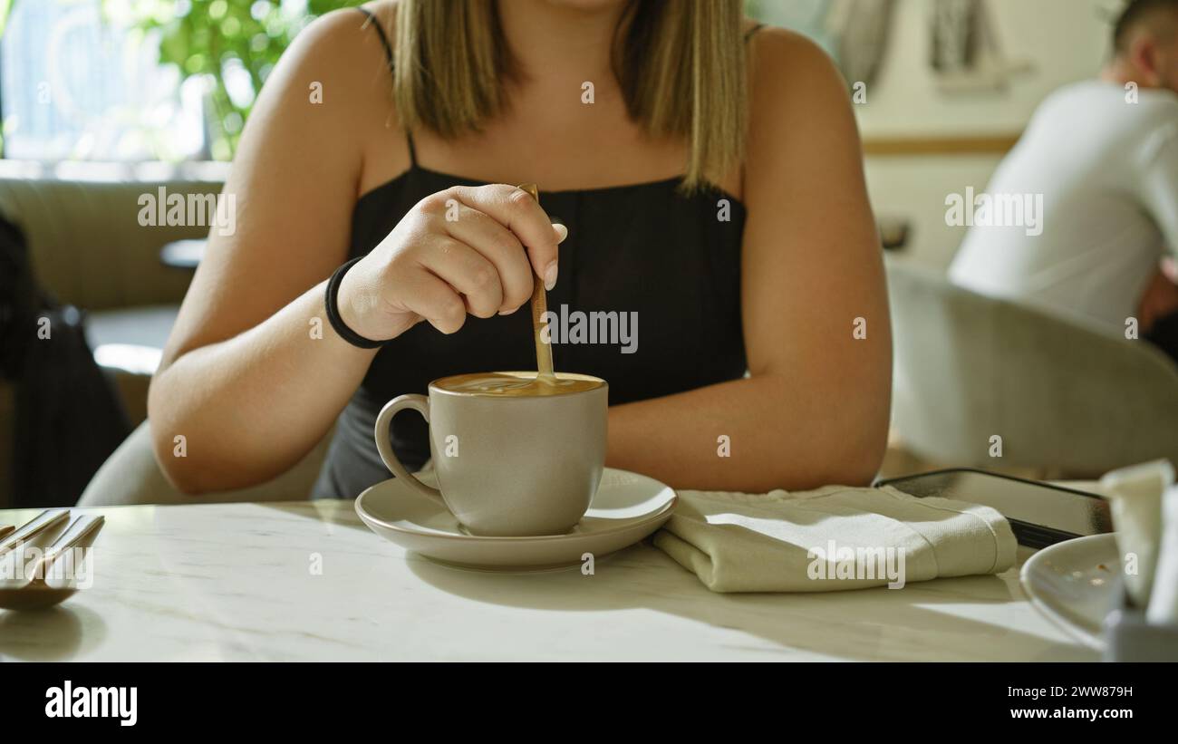 A woman stirs coffee at a restaurant table, depicting a casual dining ...