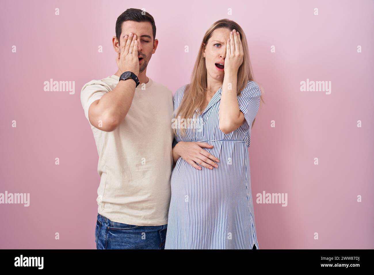 Young couple expecting a baby standing over pink background yawning ...