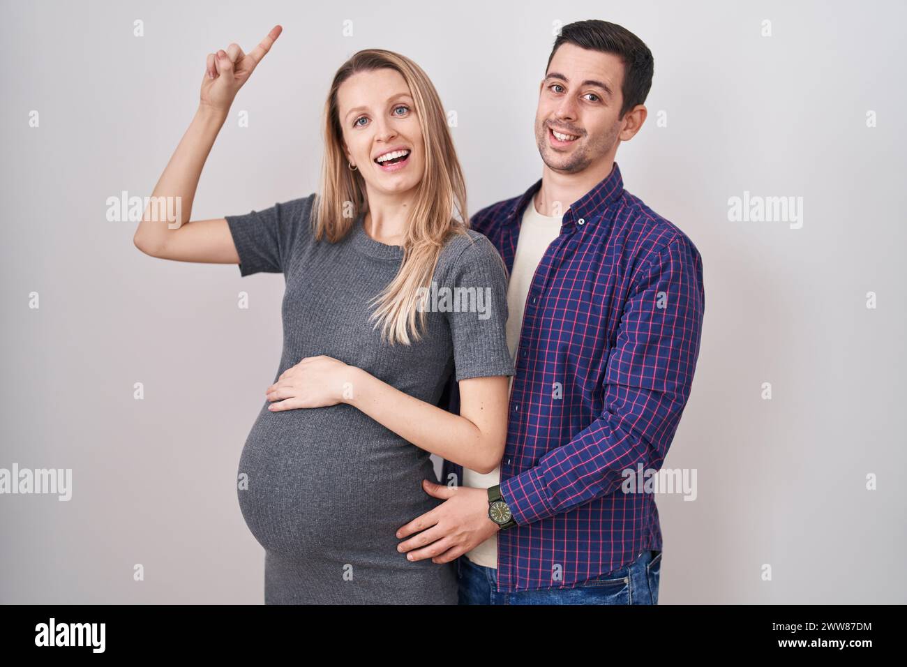 Young couple expecting a baby standing over white background smiling ...
