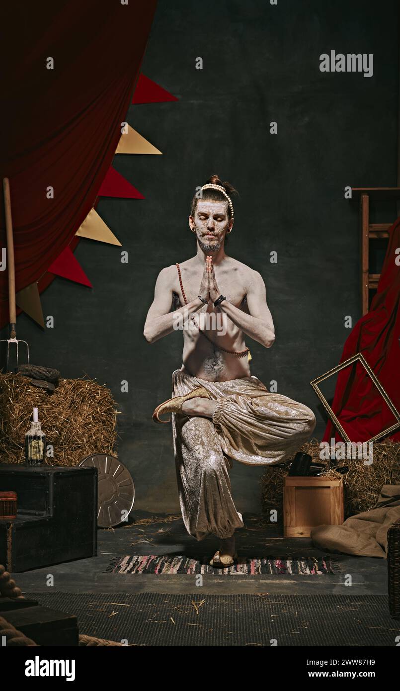 Pale man, yogi performing over dark retro circus backstage background ...